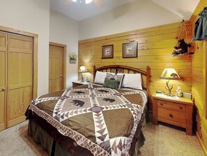 Quarto com cabeceira de madeira, colcha acolchoada, duas luminárias de cabeceira e mesa de cabeceira com abajur.