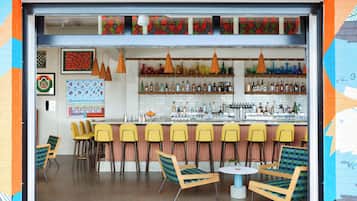 Uma área de bar com diversas opções de assentos, incluindo banquetas e cadeiras, e variedade de garrafas e copos nas prateleiras.