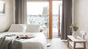 Quarto de hotel com cama, mesa de cabeceira com um vaso e vista para o exterior.
