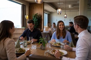 Um grupo de pessoas jantando em um restaurante com mesa de madeira, copos e luminárias pendentes.