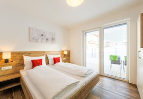 Quarto com cabeceira de madeira, cama grande com roupa de cama branca, duas almofadas vermelhas e uma obra de arte pendurada na parede.