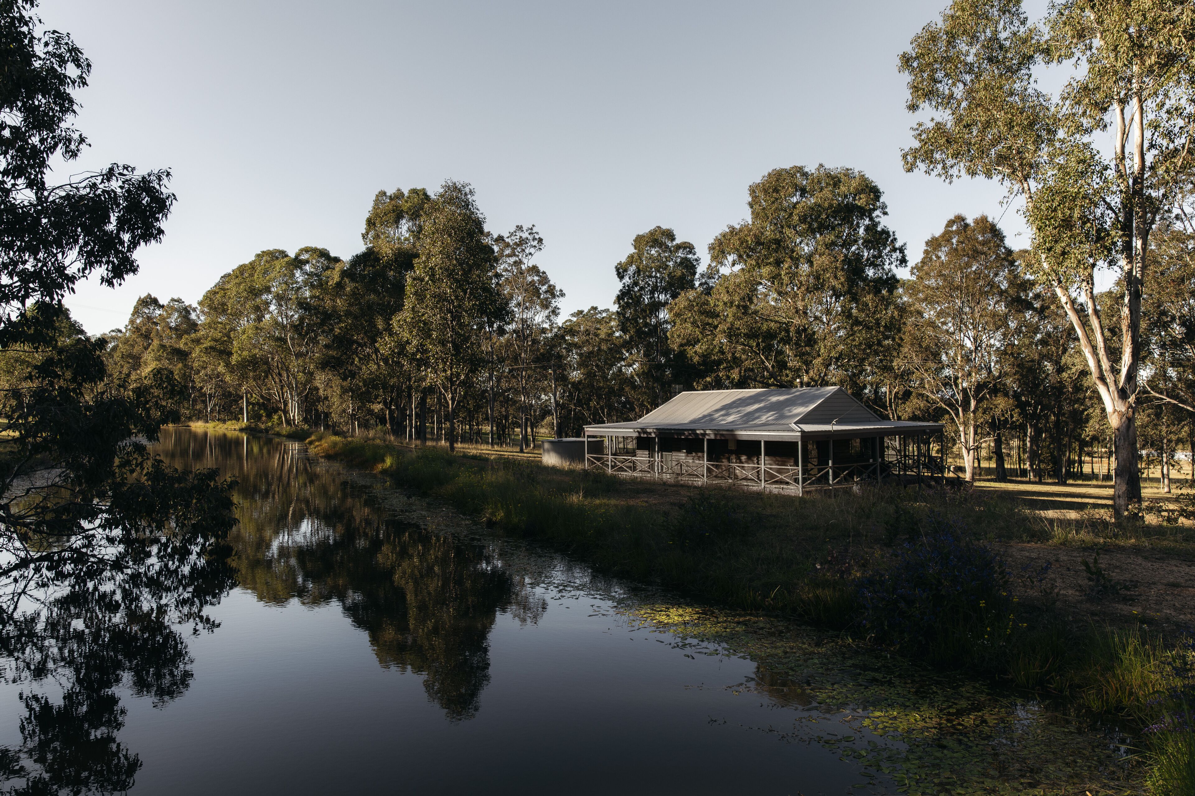 Um pavilhão à beira do lago, com telhado, cercado por árvores e um corpo d'água tranquilo.