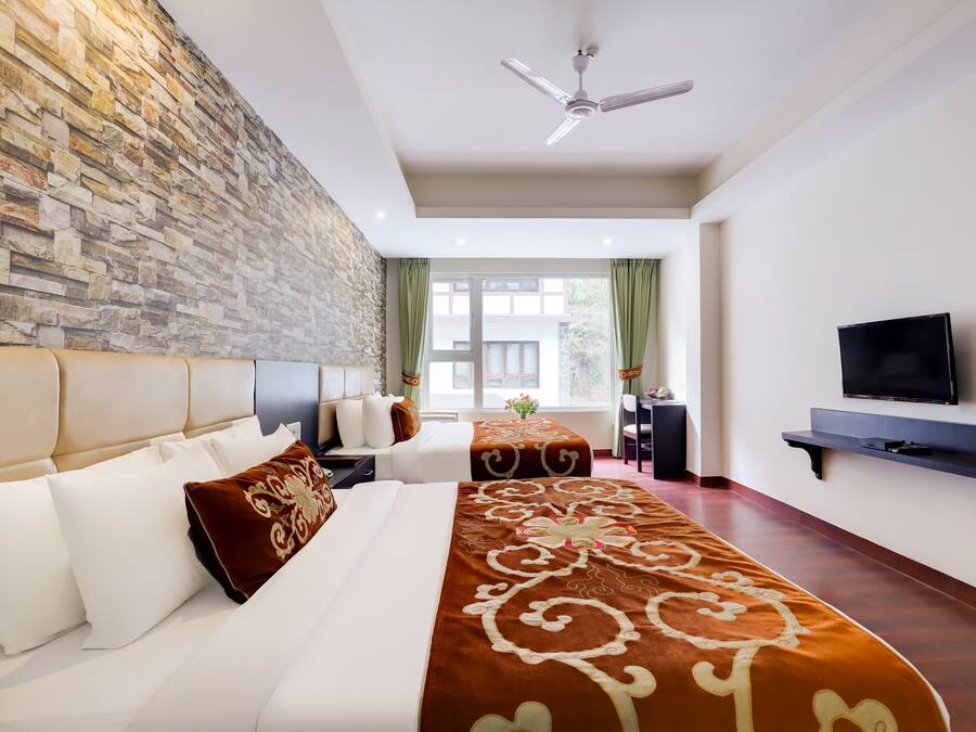 Quarto de hotel moderno com parede de destaque em pedra, uma cama grande com manta estampada, televisão de tela plana e varanda com vista.