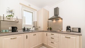 Cozinha moderna com armários de madeira clara, exaustor de aço inoxidável e janela que oferece luz natural.