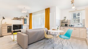 Uma sala de estar moderna com sofá, mesa de jantar com cadeiras, televisão e área de cozinha com armários e janela.