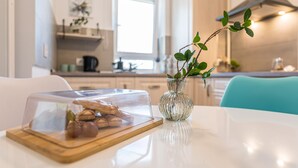 Cozinha com uma vitrine de vidro transparente contendo pão e uvas, um vaso de vidro com uma planta, e uma janela que proporciona luz natural.