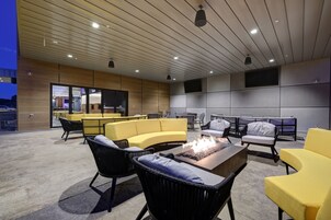 Uma área de estar moderna ao ar livre, com mobiliário amarelo e preto, lareira e uma televisão fixada na parede.