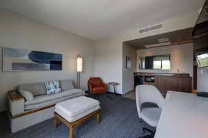 Quarto de hotel moderno com sofá, poltrona, banqueta e pequena mesa de jantar.