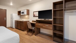 Quarto de hotel compacto com cama, cozinha compacta, escrivaninha e estantes embutidas.