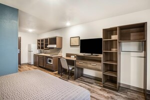 Quarto de hotel compacto com cozinha compacta, cama, escrivaninha com cadeira, televisão e prateleiras embutidas.