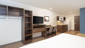 Quarto de hotel moderno e compacto, com uma cama, escrivaninha, televisão, micro-ondas e frigorífico.