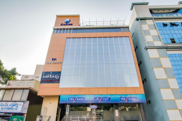 Um edifício com uma grande fachada de vidro, um letreiro com 'The Centre' no topo e placas 'YES BANK' na parte inferior.