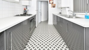 Cozinha moderna com armários brancos, piso com padrão preto e branco, fogão a gás e pia de aço inoxidável.