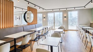 Uma sala de jantar moderna com mesas e cadeiras longas, lambris de madeira e grandes janelas.