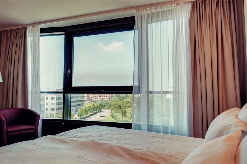 Quarto de hotel com uma janela grande, uma cama e uma cadeira.