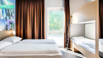 Quarto de hotel com uma cama grande, uma cama menor, uma escrivaninha e uma janela com cortinas.