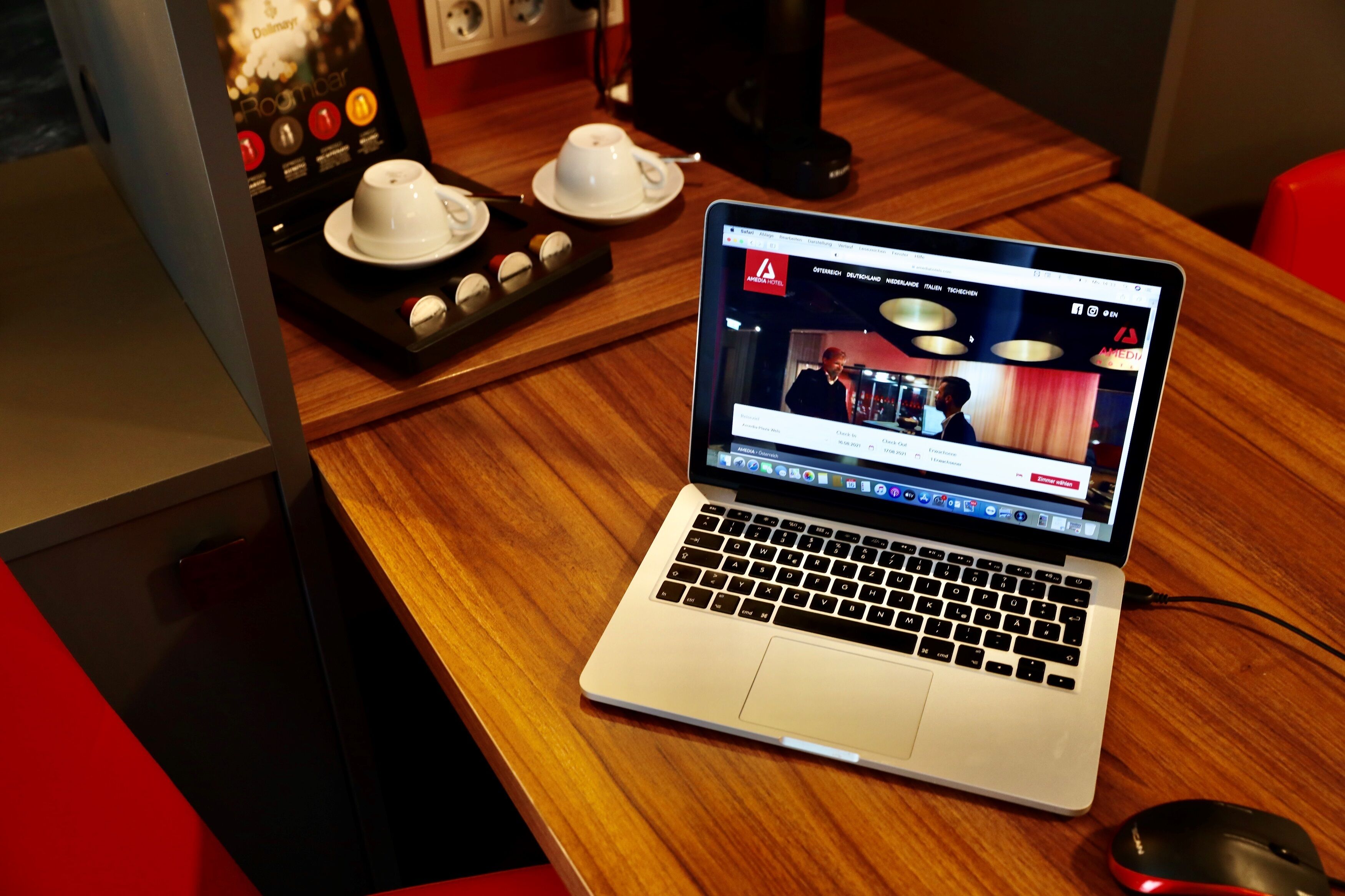 Um laptop sobre uma mesa de madeira, com uma máquina de café e xícaras por perto.