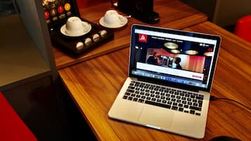 Um laptop sobre uma mesa de madeira, com uma máquina de café e xícaras por perto.