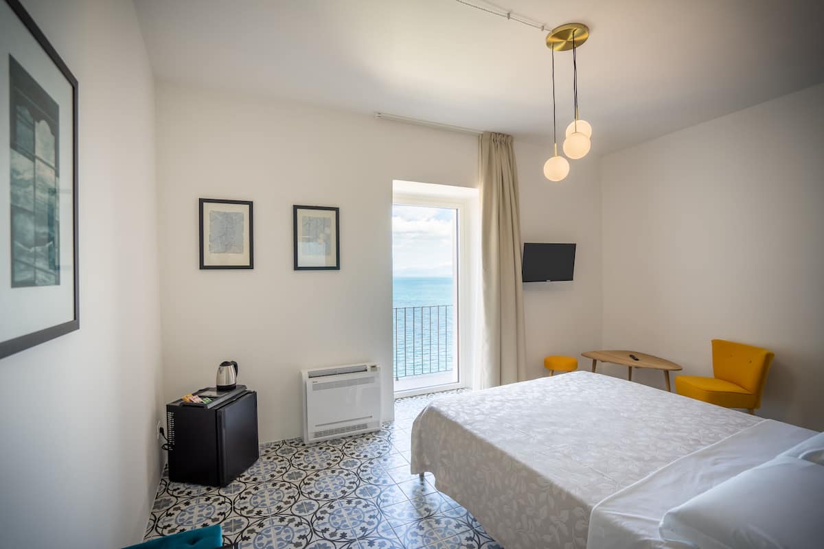 Quarto de hotel com cama, escrivaninha, cadeira, aquecedor, mala e televisão na parede.