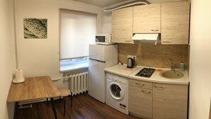 Uma cozinha compacta com máquina de lavar, micro-ondas, pia e uma pequena mesa.