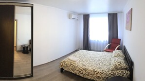Quarto de hotel com cama, televisão, cadeira, espelho e janela com cortinas.