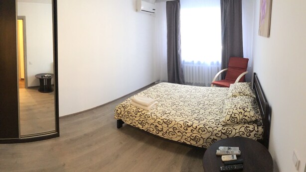 Quarto de hotel com cama, televisão na parede, cadeira, mesa pequena e janela com cortinas.