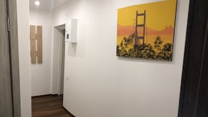 Um corredor com piso de madeira, uma porta branca e um quadro de uma ponte.
