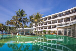 Um hotel com piscina, palmeiras e um edifício de vários andares.