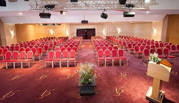 Uma sala de conferências com fileiras de cadeiras vermelhas, um púlpito e um palco.