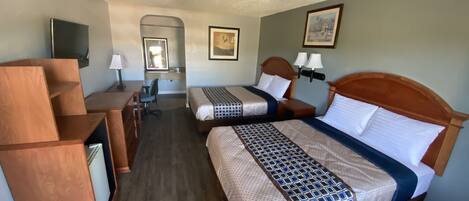 Quarto de hotel com duas camas, uma mesa de trabalho, uma cadeira, televisão e banheiro com espelho.