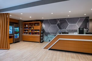 Uma área de recepção moderna com balcão de madeira, uma vitrine refrigerada e uma parede com padrão hexagonal.