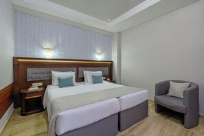 Quarto de hotel com uma cama grande, duas mesas de cabeceira, uma cadeira e luminária na parede.