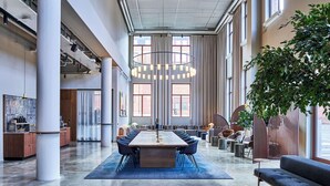 Uma sala de conferências ampla com uma mesa comprida, cadeiras e um lustre moderno.