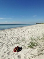 Uma praia arenosa com pegadas e um par de sapatos vermelhos e pretos.