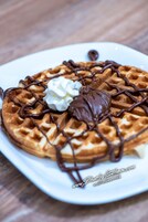 Waffle com calda de chocolate e chantilly em um prato.