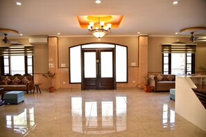 Um hall amplo com piso lustroso, um lustre central e uma porta de madeira.