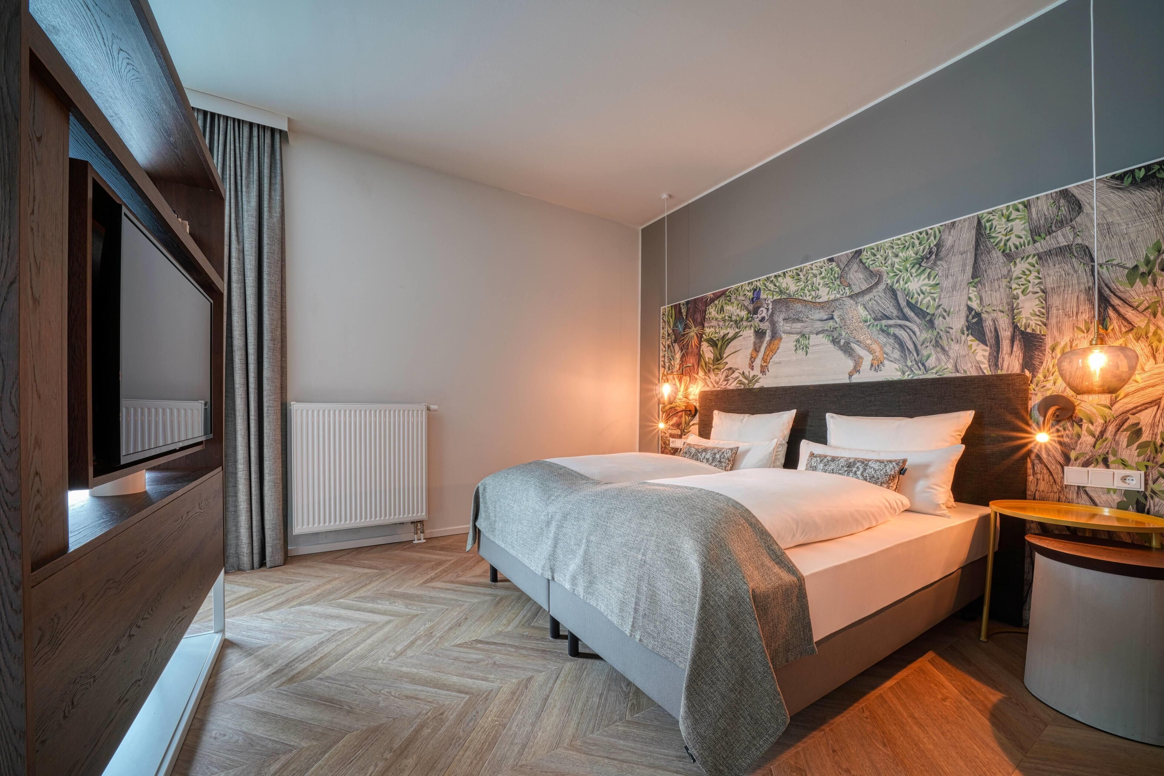 Quarto de hotel moderno com uma cama grande, televisão, um mural na parede e piso de madeira.