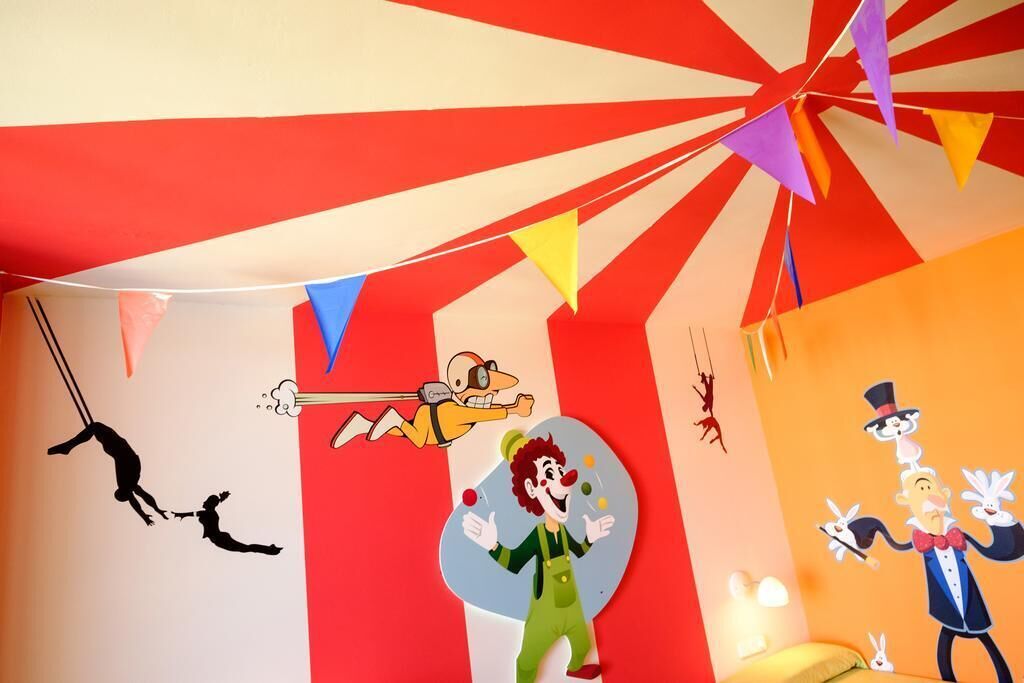 Quarto com teto listrado em vermelho e branco, um palhaço e um personagem equilibrando coelhos.