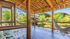 Um deck de madeira com uma rede e cadeiras de descanso, com vista para um jardim tropical cheio de palmeiras.