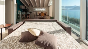 Quarto moderno com cama grande, duas almofadas e vista para uma sala de jantar e paisagem panorâmica.