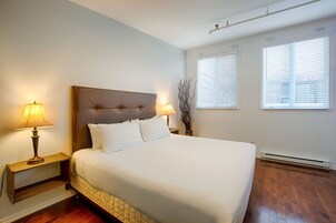Uma cama bem arrumada com roupa de cama branca, duas luminárias de cabeceira e uma mesa de cabeceira de madeira.