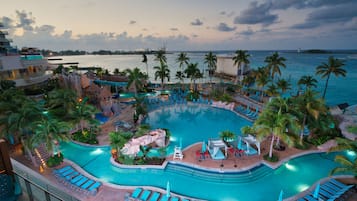 Uma piscina grande e sinuosa com várias áreas de estar e palmeiras, rodeada por um edifício de resort.