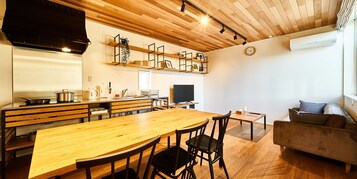 Uma cozinha moderna com armários de madeira, uma mesa grande de madeira e cadeiras. Há um sofá e uma pequena mesa na sala de estar.