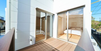 Quarto moderno com grande porta de vidro deslizante, deck de madeira e vista da região ao redor.