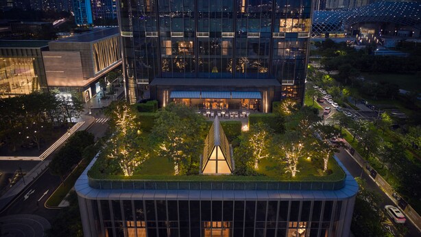 Um edifício moderno com um jardim no terraço, um caminho central e vegetação ao redor.