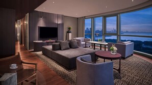 Uma sala de estar moderna com uma televisão grande, assentos confortáveis, um espaço de refeições e vista para o horizonte da cidade.