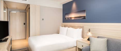 Quarto de hotel com cama, mesa de cabeceira, televisão e sofá.