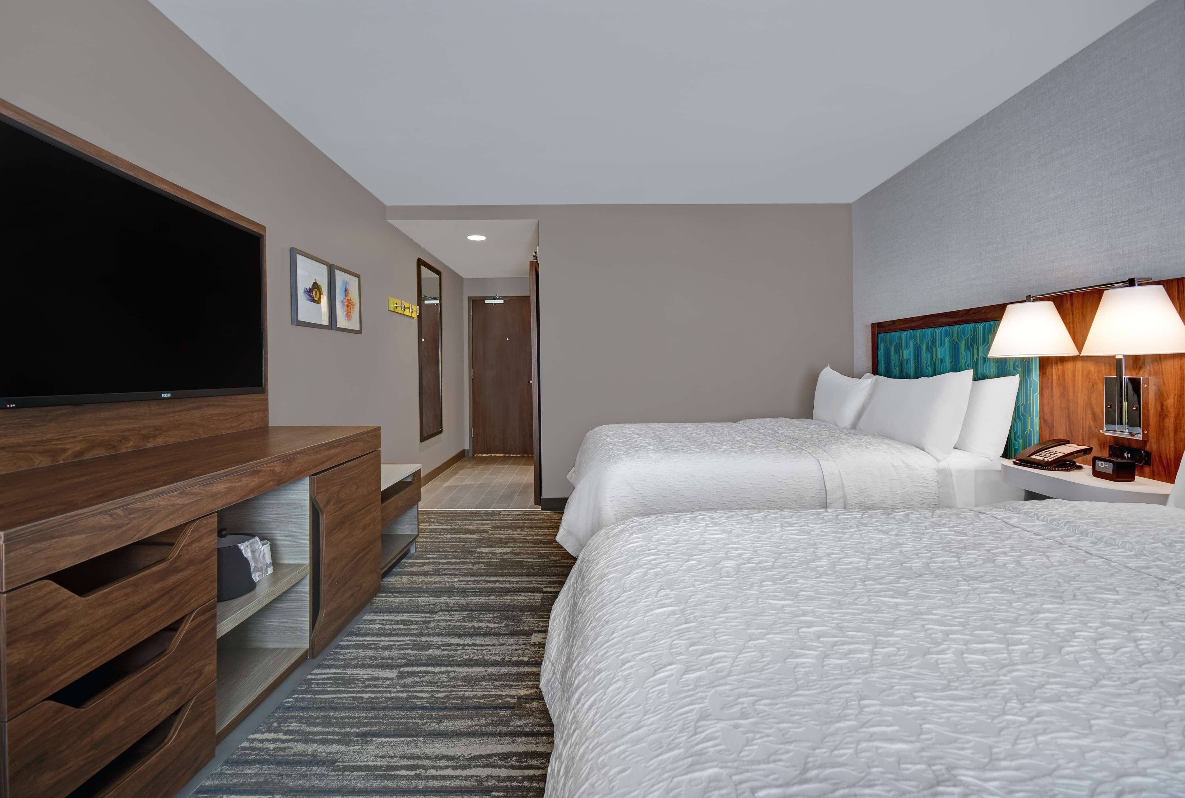 Quarto de hotel com duas camas, televisão, escrivaninha e luminária.