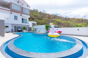 Piscina com flutuador de fonte, cercada por um edifício moderno com varandas e área ajardinada.