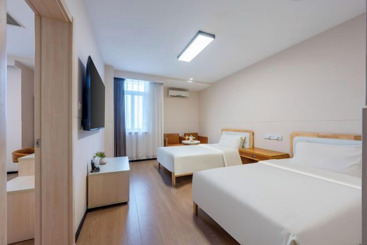 Quarto de hotel com duas camas, televisão, escrivaninha e janela com cortinas.
